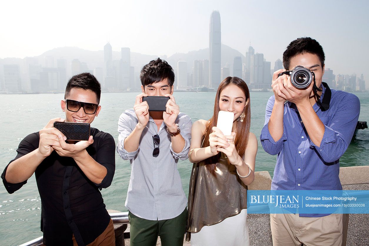 Fashionable young Chinese friends photographing with smart phones and ...